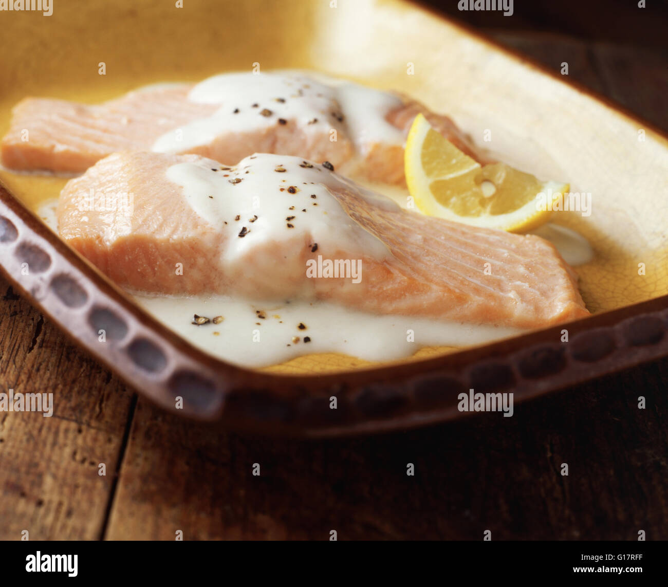 Baked salmon with bechamel sauce and lemon wedge in ceramic baking tin ...
