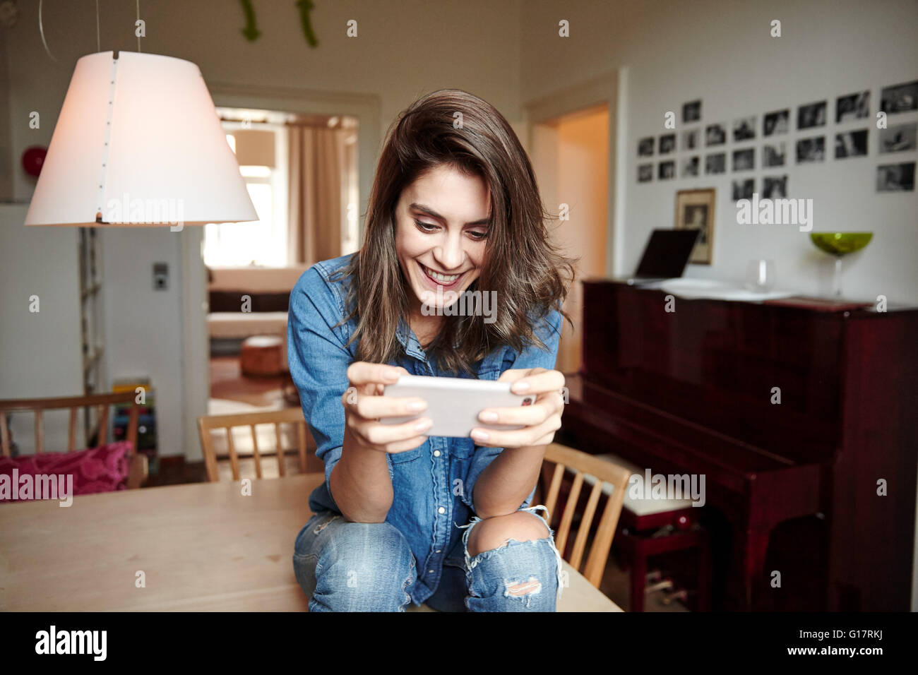 Young woman sitting on dining table reading smartphone texts Stock ...