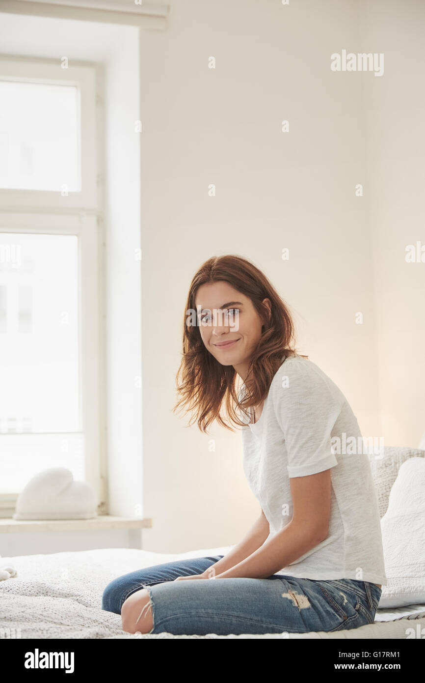 Portrait of young woman kneeling on bed Stock Photo - Alamy