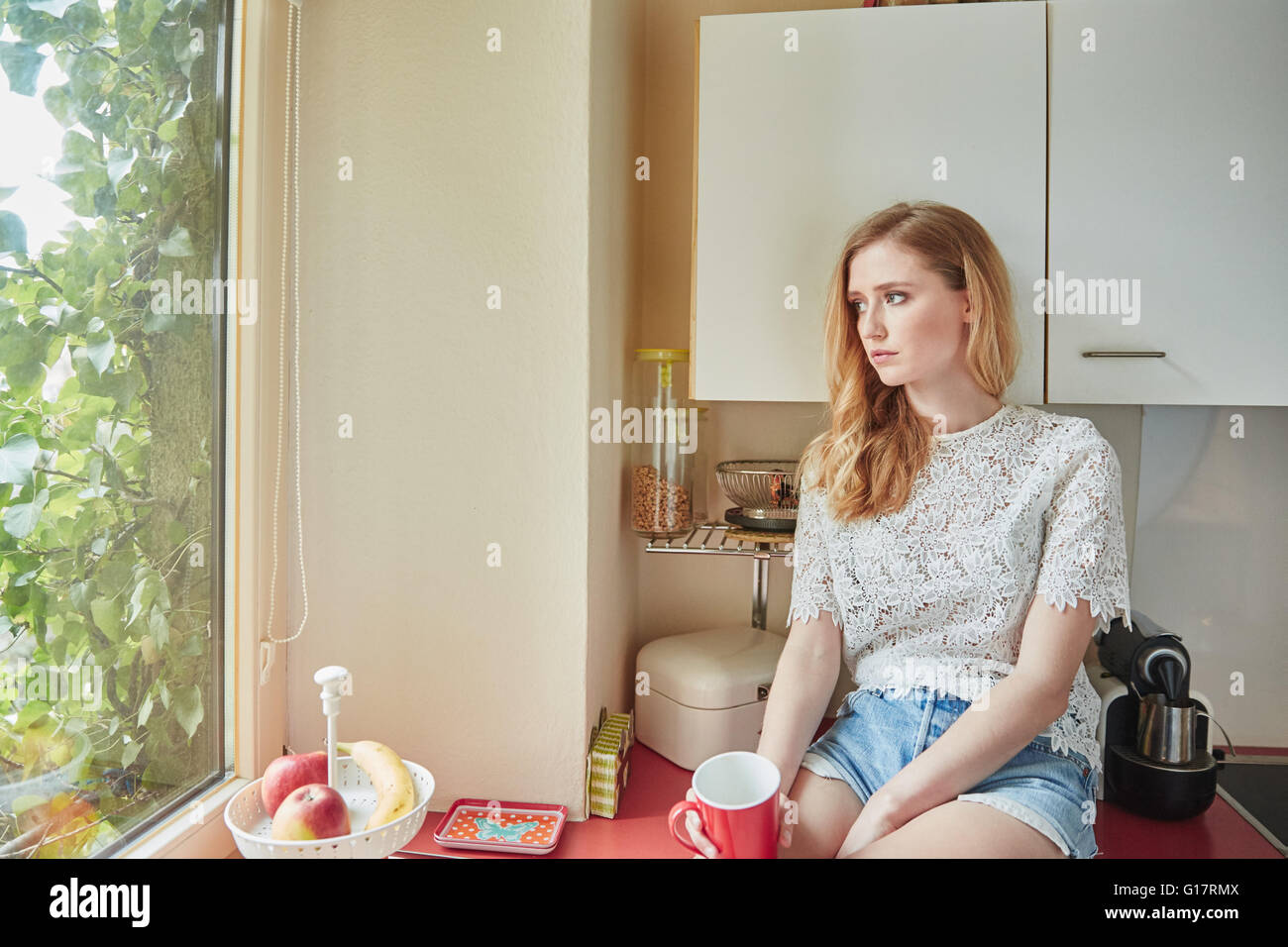 Young woman looking through window from kitchen counter Stock Photo - Alamy
