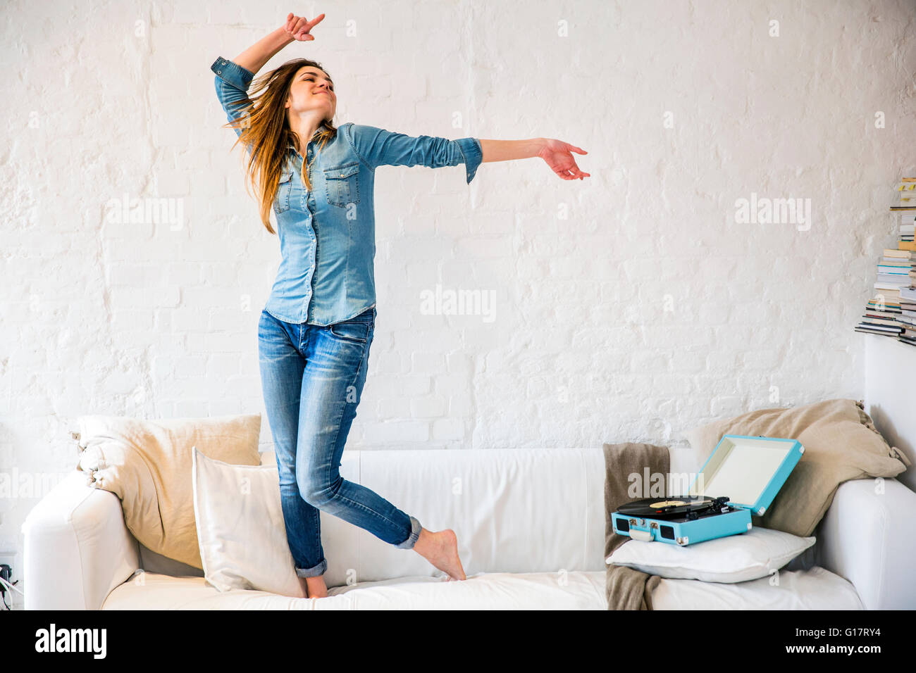 Young woman standing on sofa dancing to vintage record player Stock ...
