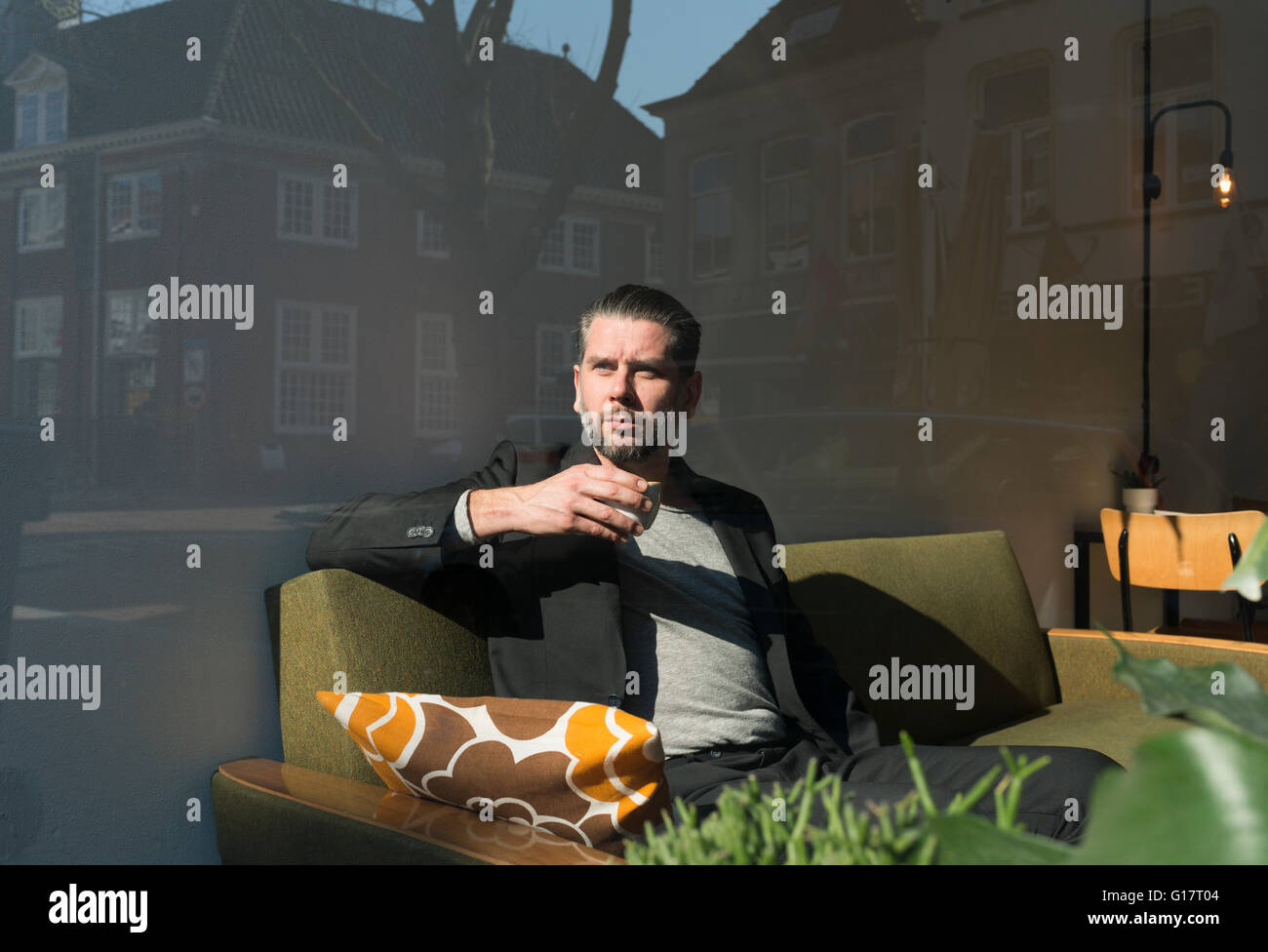 Window view of cool man sitting on retro cafe sofa looking through ...