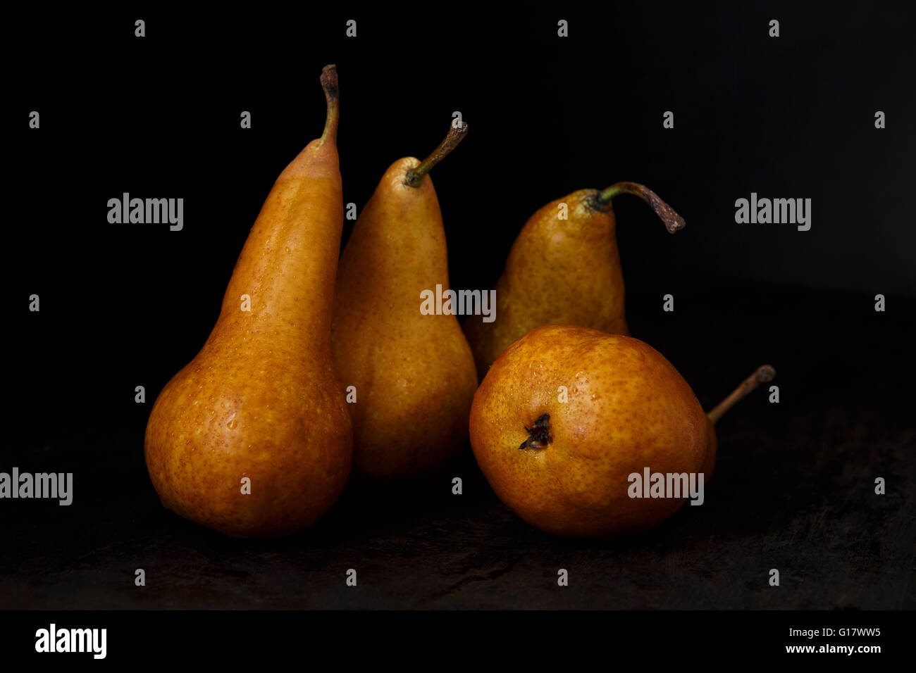 Four golden-brown pears with little tails on a black background Stock ...