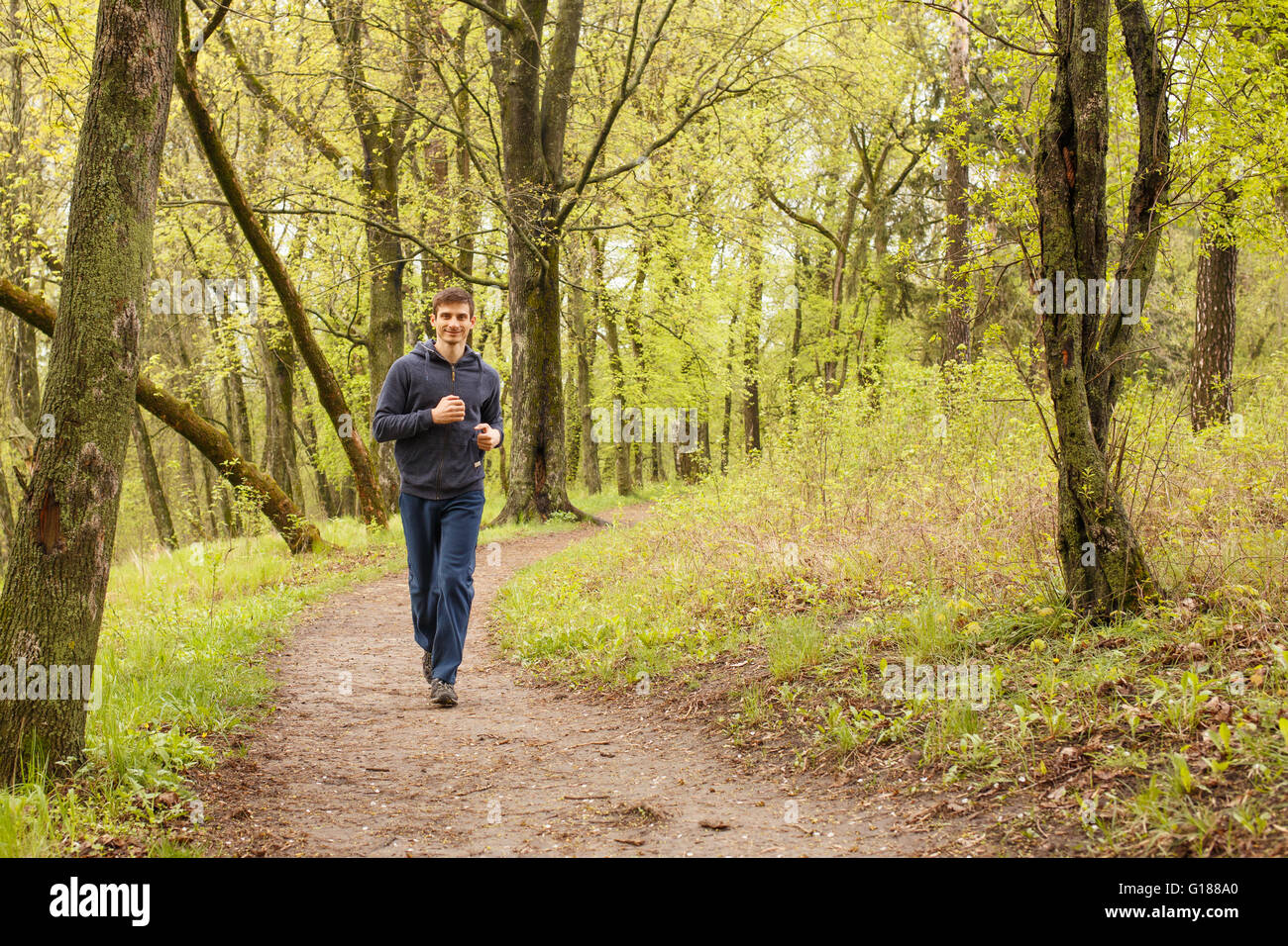 Young sporty man jogging in the morning forest. Trail runner in spring ...