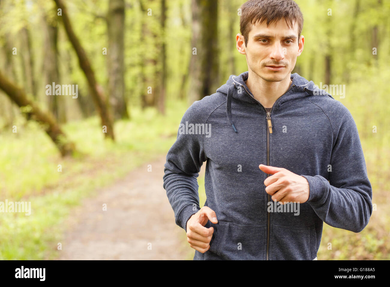 Young sporty man jogging in the morning forest. Trail runner in spring ...