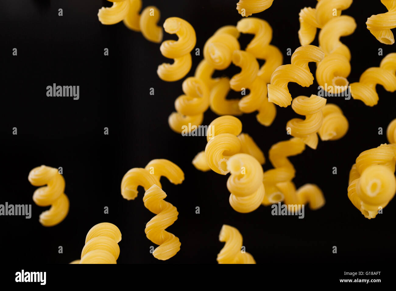 Falling cavatappi pasta. Flying yellow raw macaroni over black ...