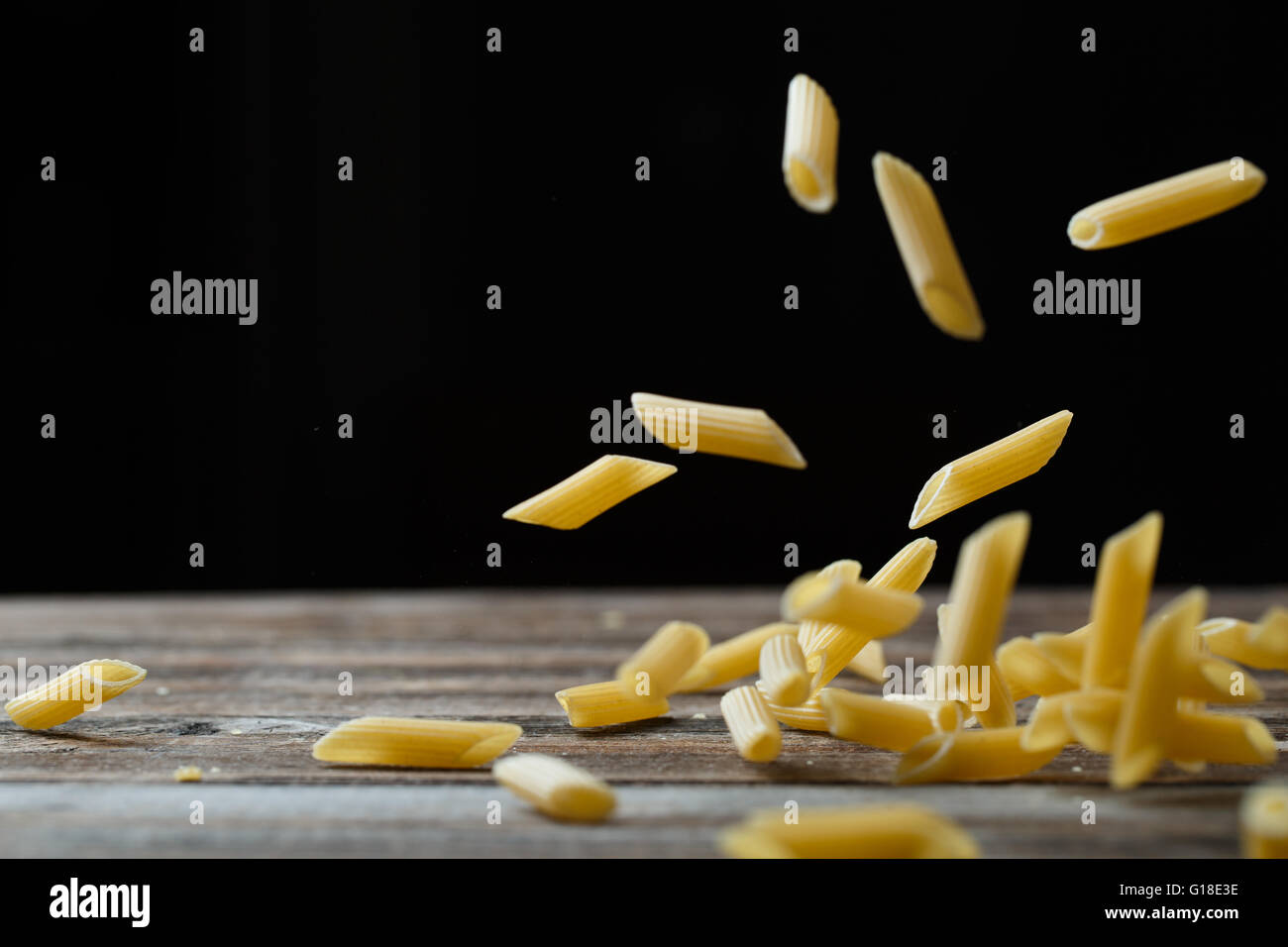 Falling penne pasta. Flying yellow raw macaroni over black background ...