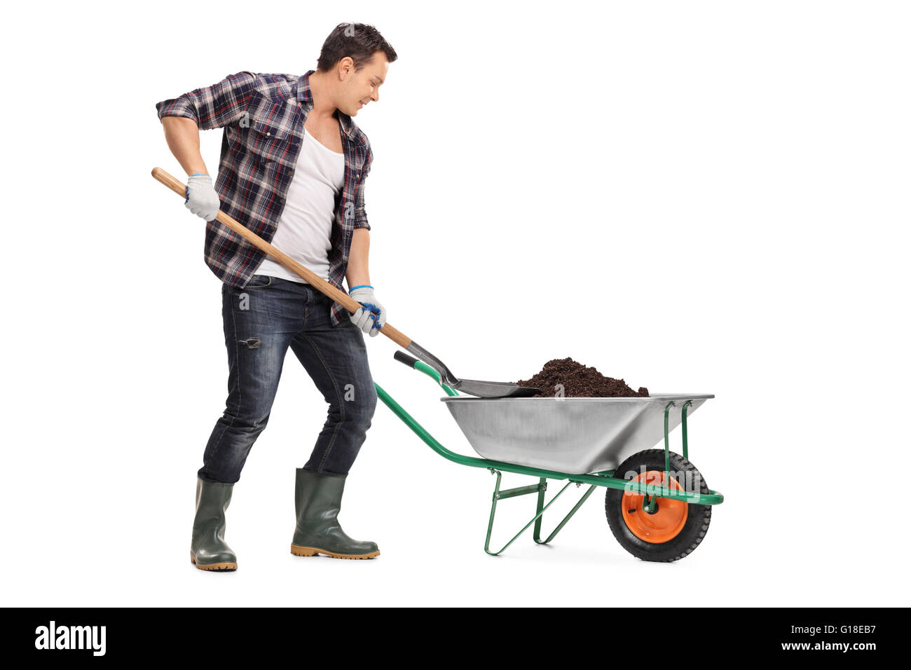 Young worker loading dirt into a wheelbarrow with a shovel isolated on ...