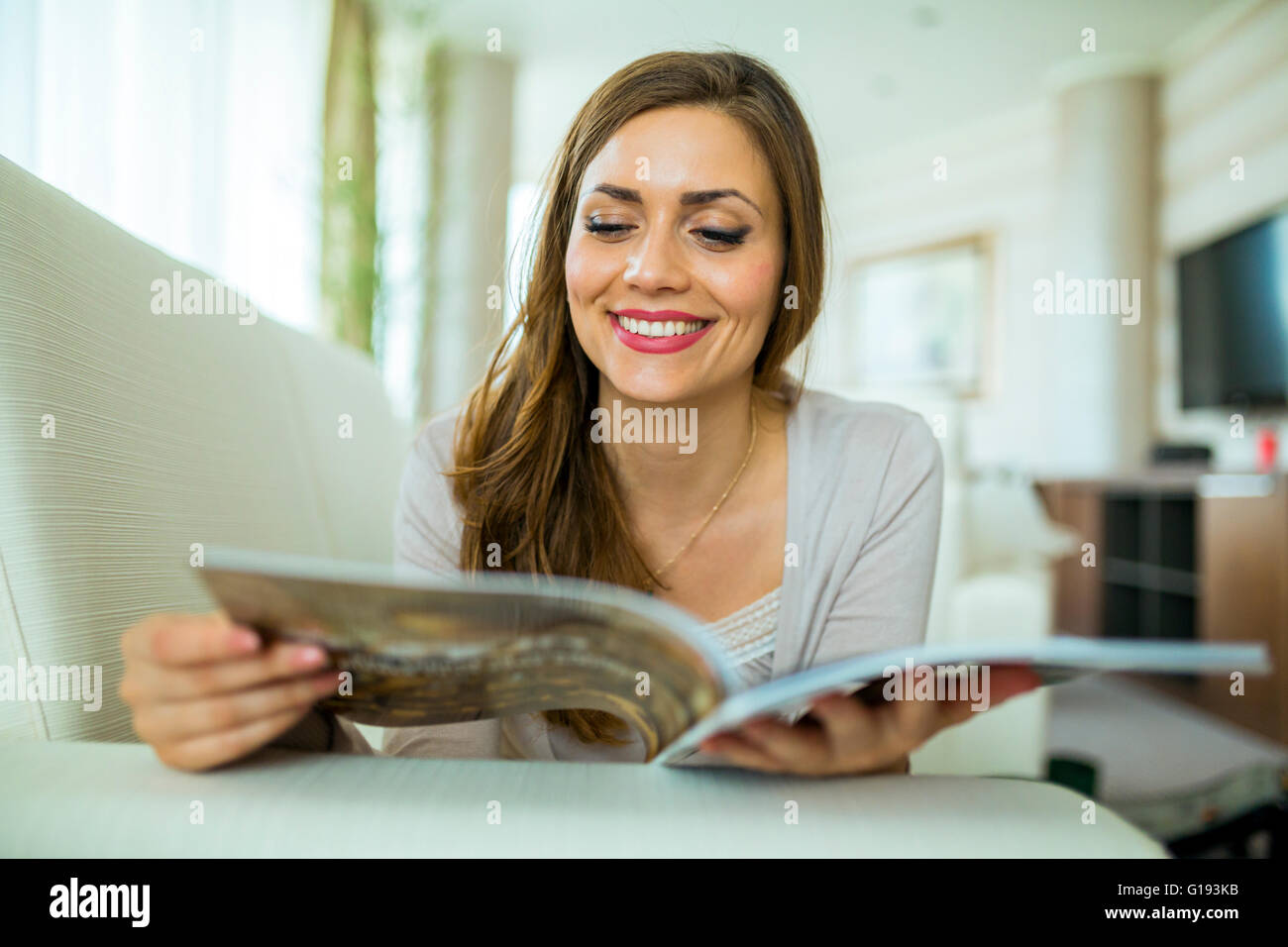 Beautiful woman on a sofa reading a paper in a well lit stylish living ...