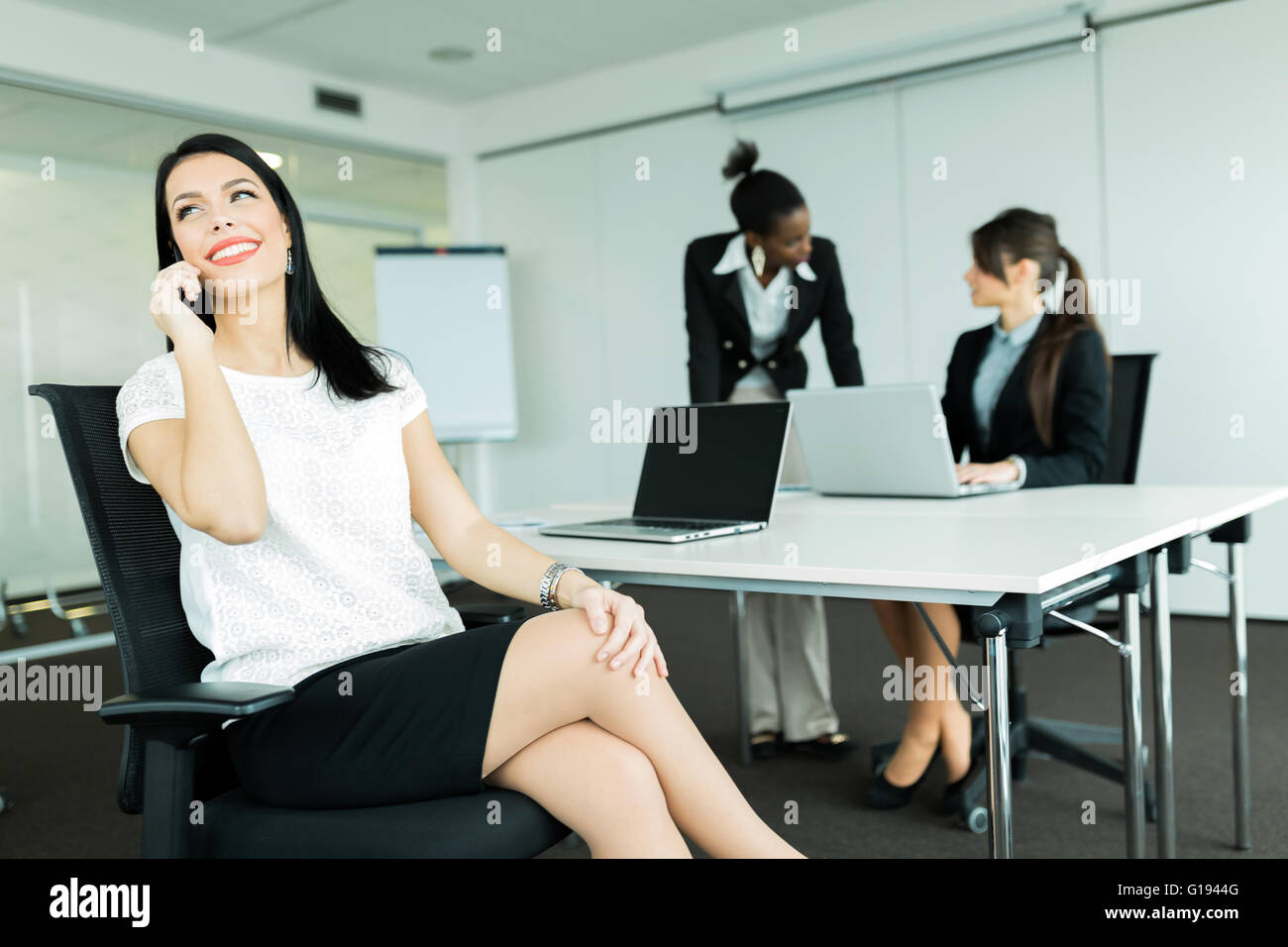 Beautiful businesswomen in an office working on a laptop and calling ...