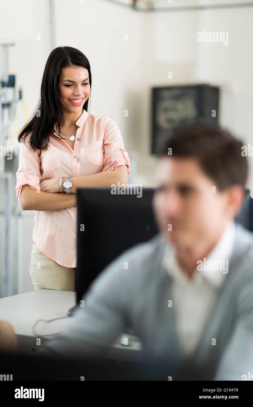 Beautiful young female teacher overseeing students' work in a classrom ...