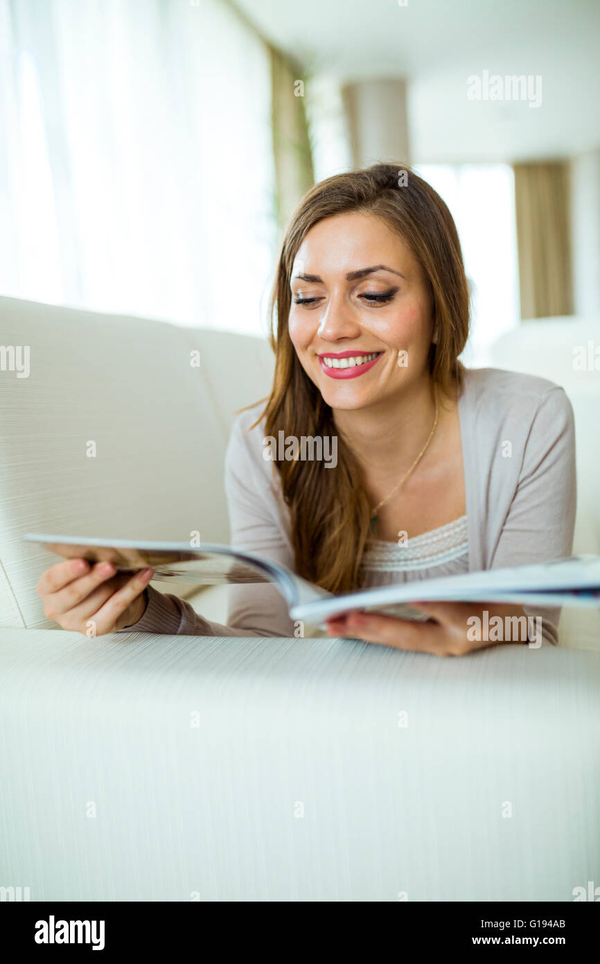Beautiful woman on a sofa reading a paper in a well lit stylish living ...