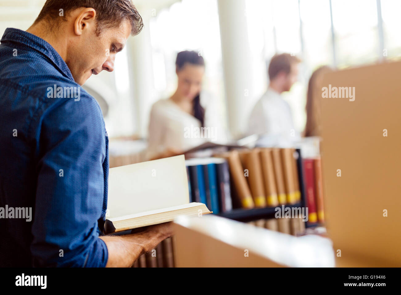Young male student reading a book amid bookshelves in the college ...