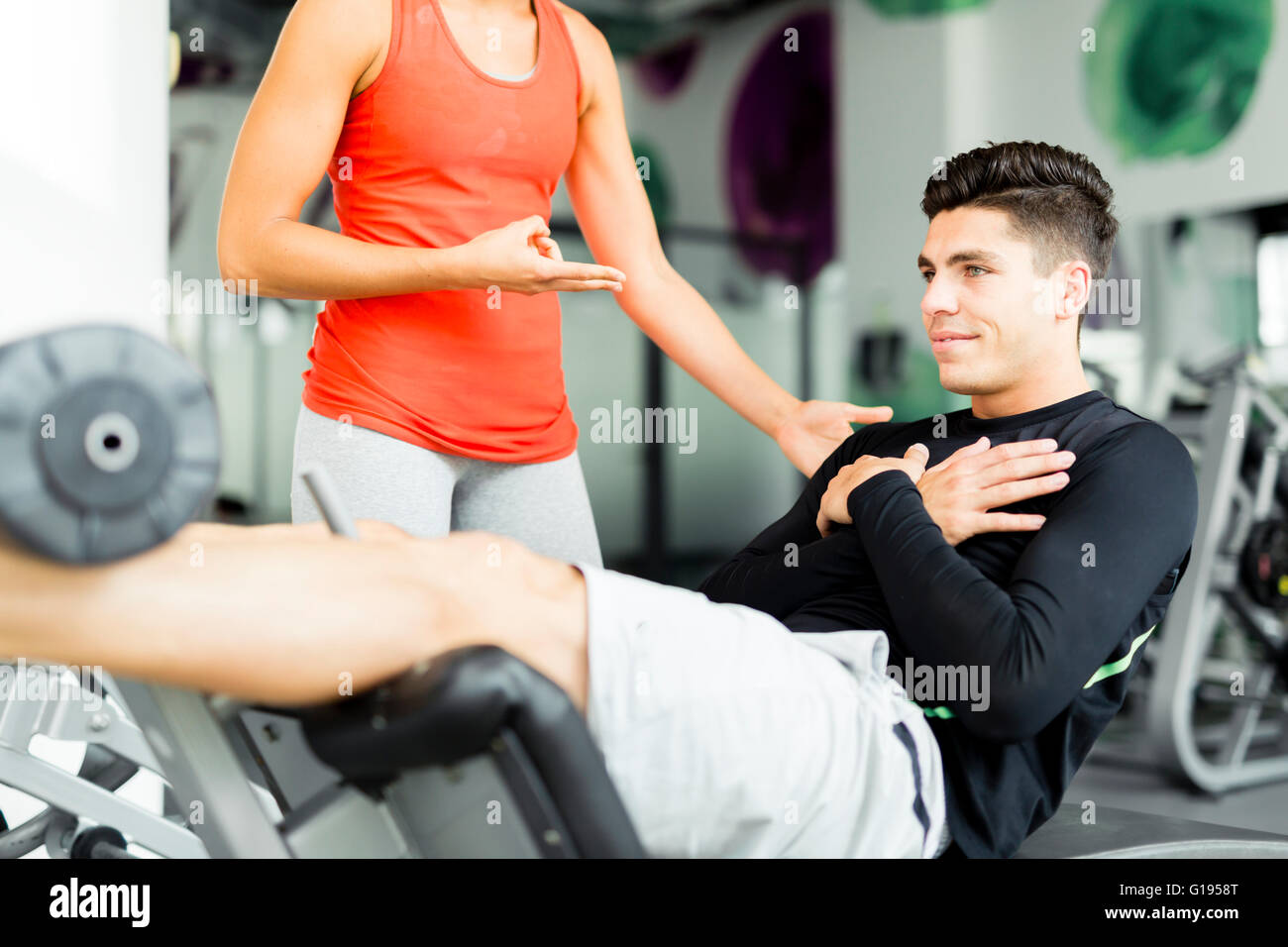 Beautiful young woman instructing a young man in the gym and ...