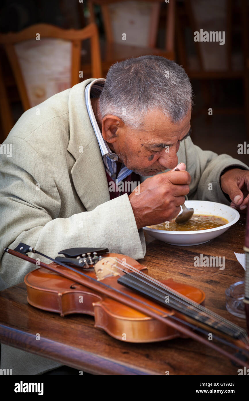 A street musician drinking soup at a restaurant table in Nessebar ...
