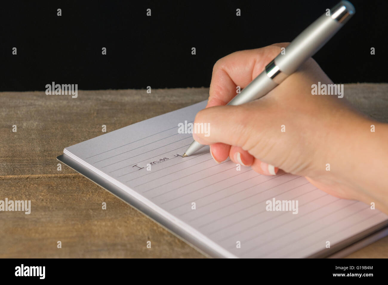 Close-up of a hand writing with a silver pen on a lined notepad, on a ...