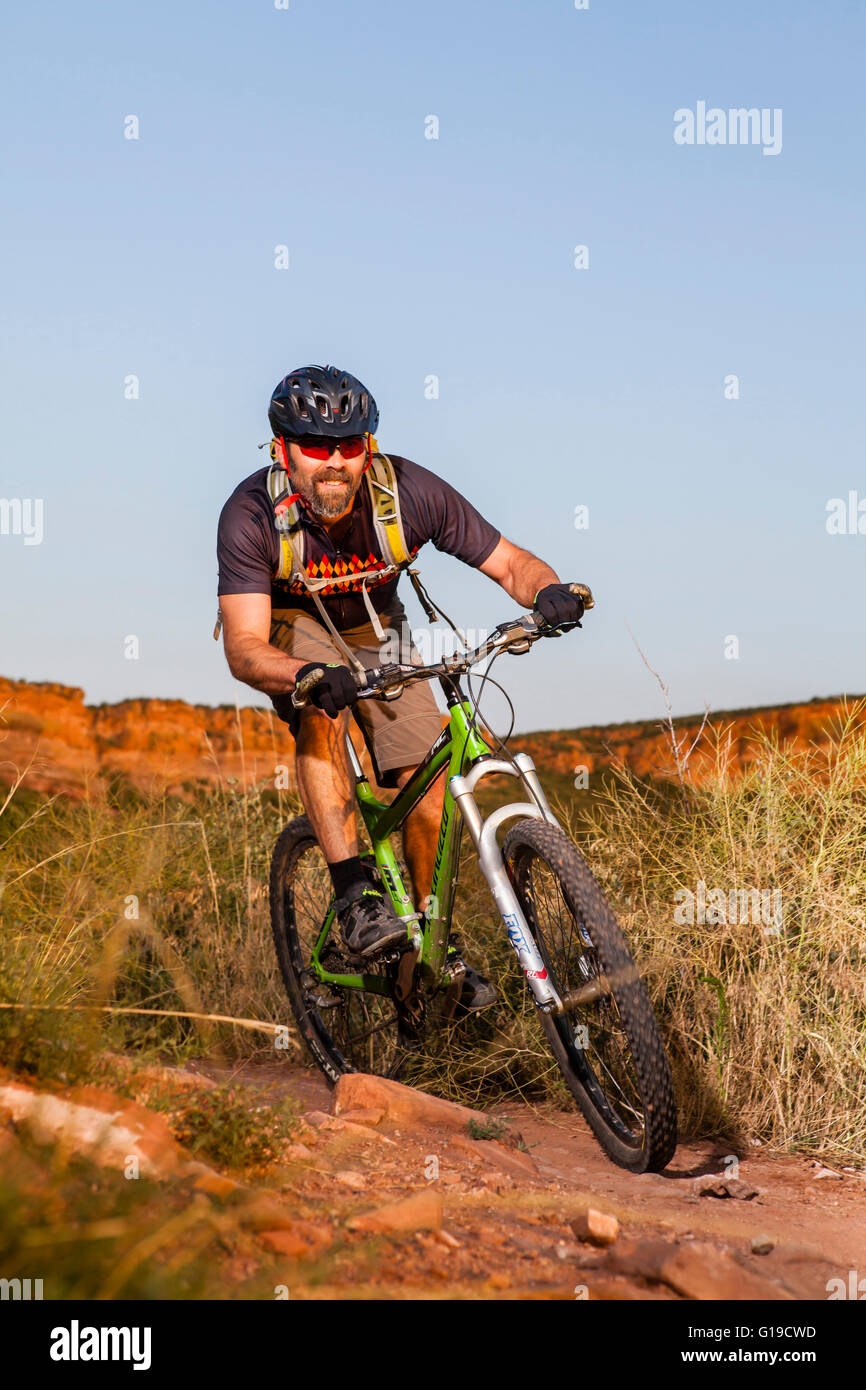 A male mountain biker rides on a single track trail among meadows and ...