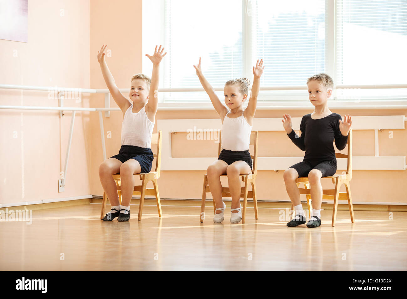 Young dancers playing or doing exercise while sitting on chairs at ...