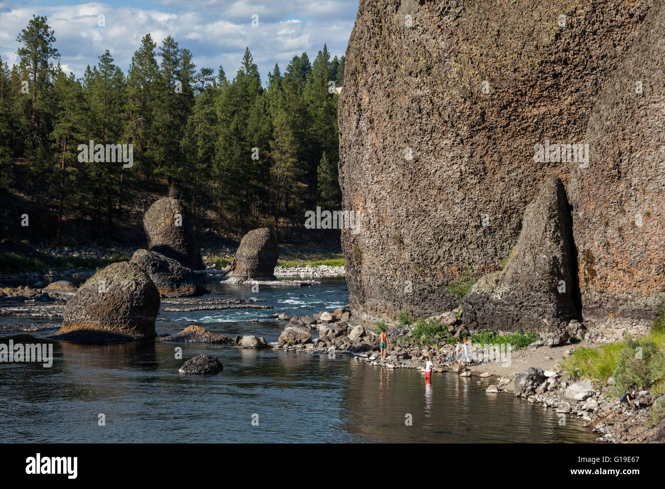 Visitors stand below tall basalt cliffs along the Spokane River ...