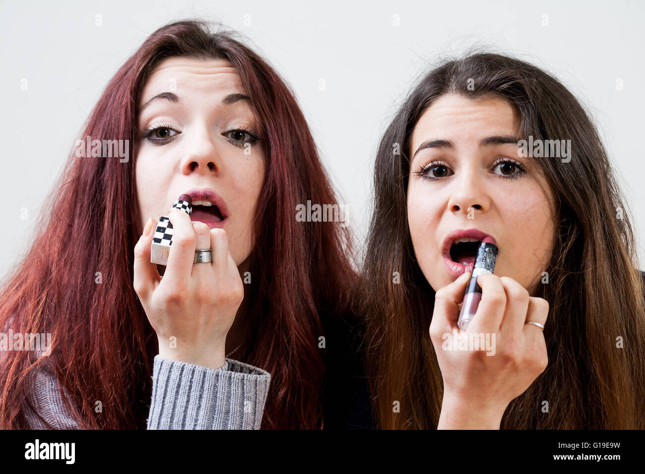 two girls applying make up together looking themselves in the mirror ...