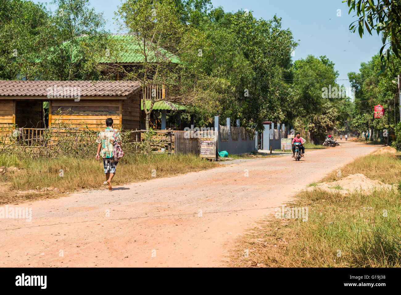 A Cambodian road wit one man walking and another one coming in on his ...