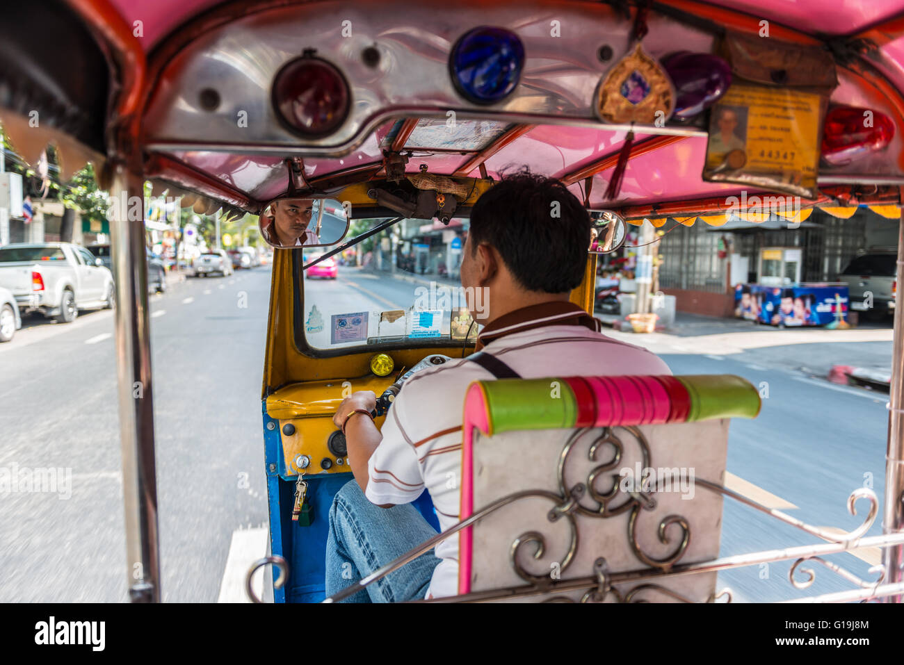 A man driving a tuk-tuk in Bangkok and looking through the mirror of ...