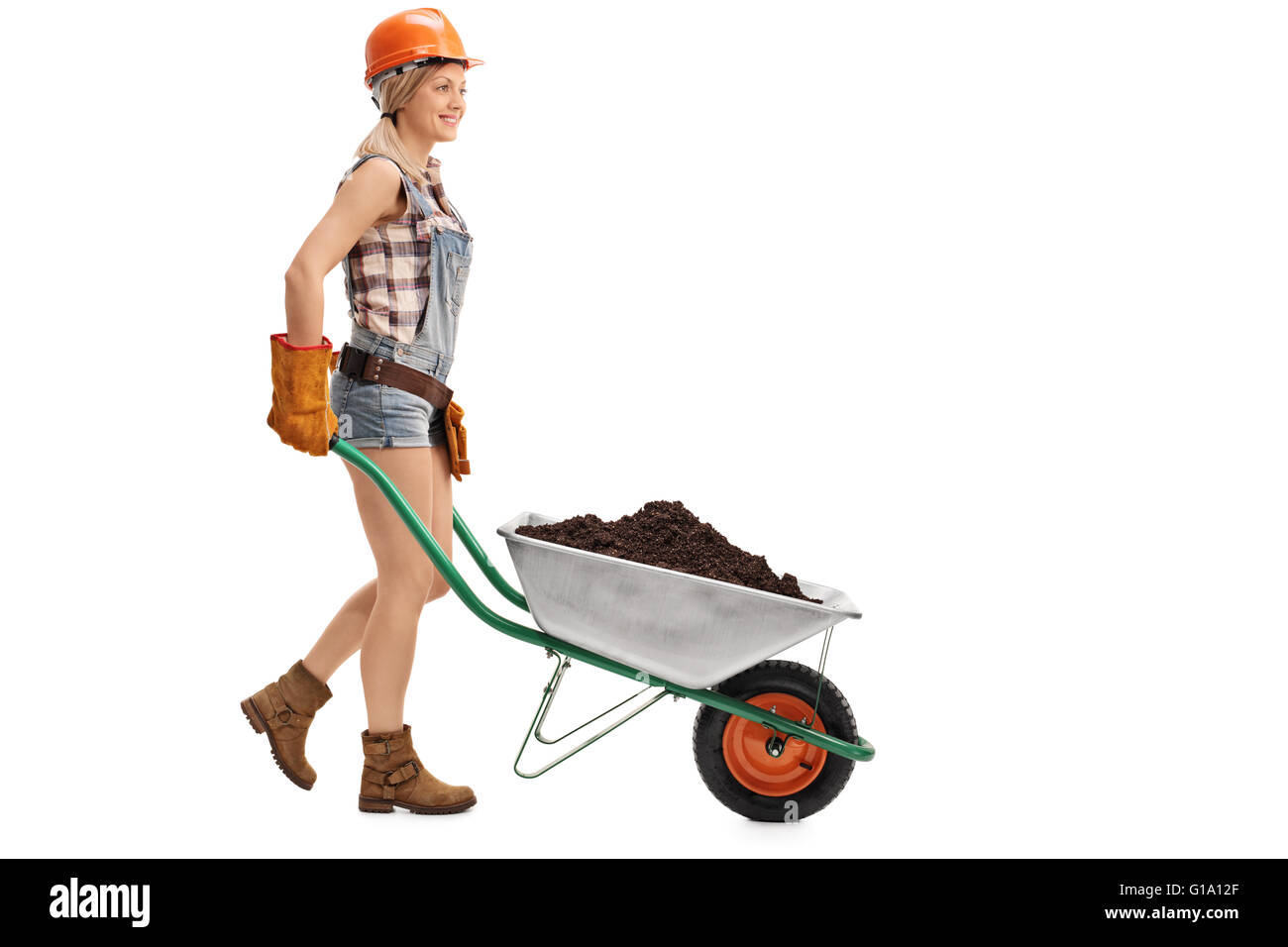 Young female construction worker pushing a wheelbarrow full of dirt ...