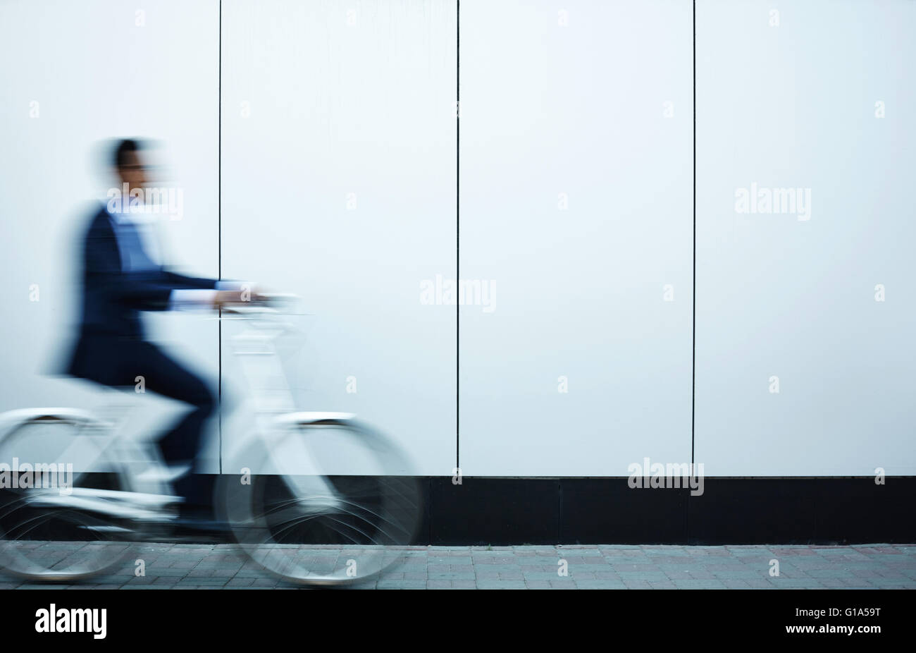 Businessman on bicycle moving along wall of modern building Stock Photo ...
