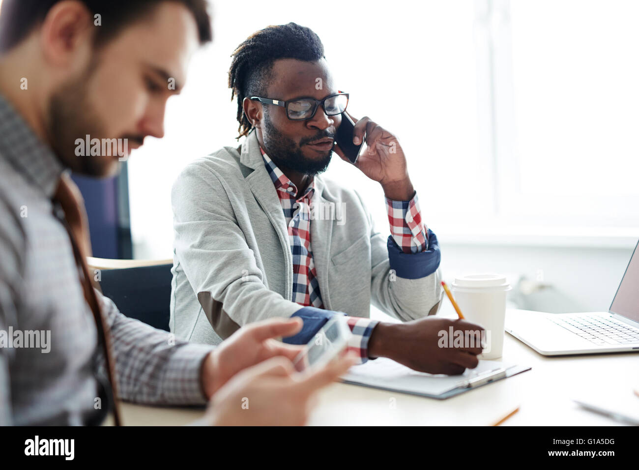 Young African employee speaking on the phone with colleague near by ...