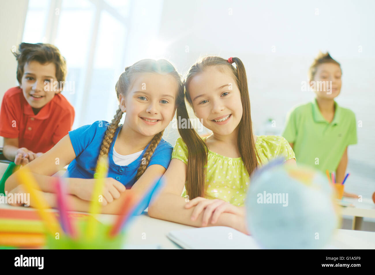 Friendly schoolgirls looking at camera on background of group-mates ...