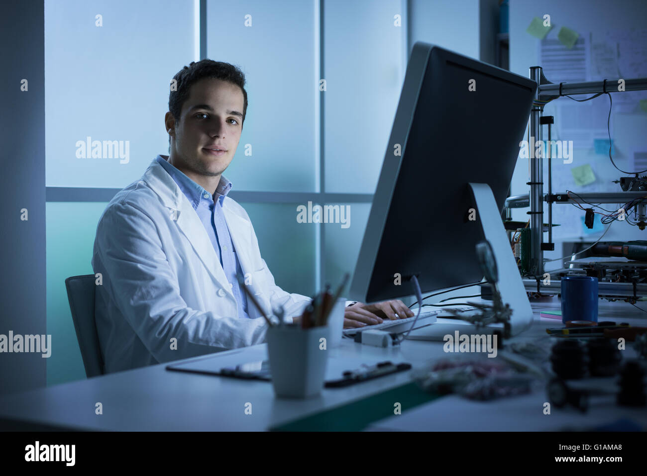Young engineer wearing a lab coat and working at desk with a computer ...