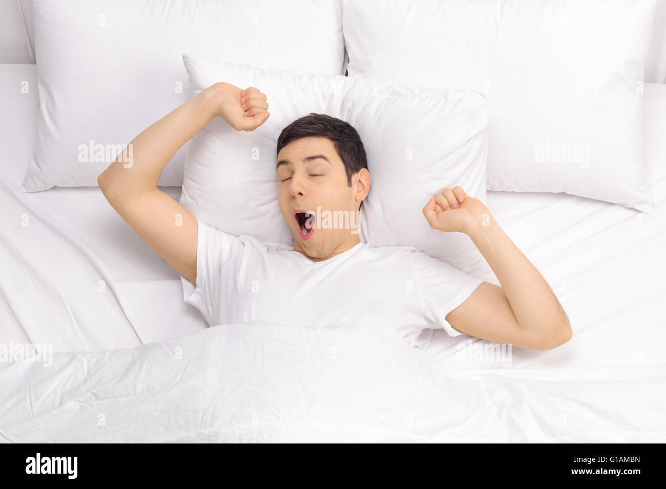 Young rested man waking up in a comfortable bed and stretching himself ...