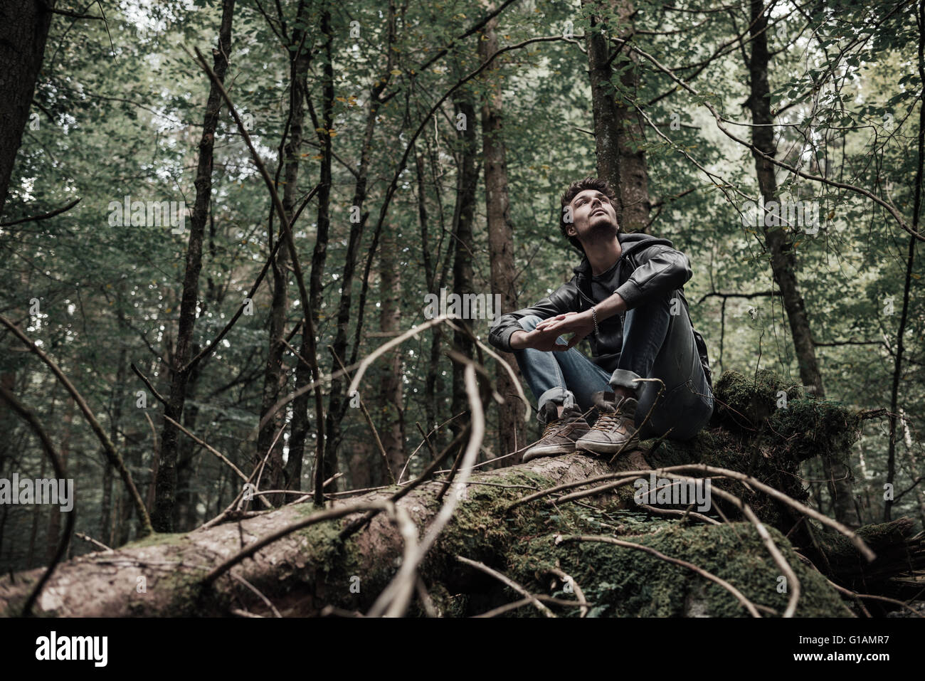 Young man sitting on a trunk in the forest and relaxing, freedom and ...