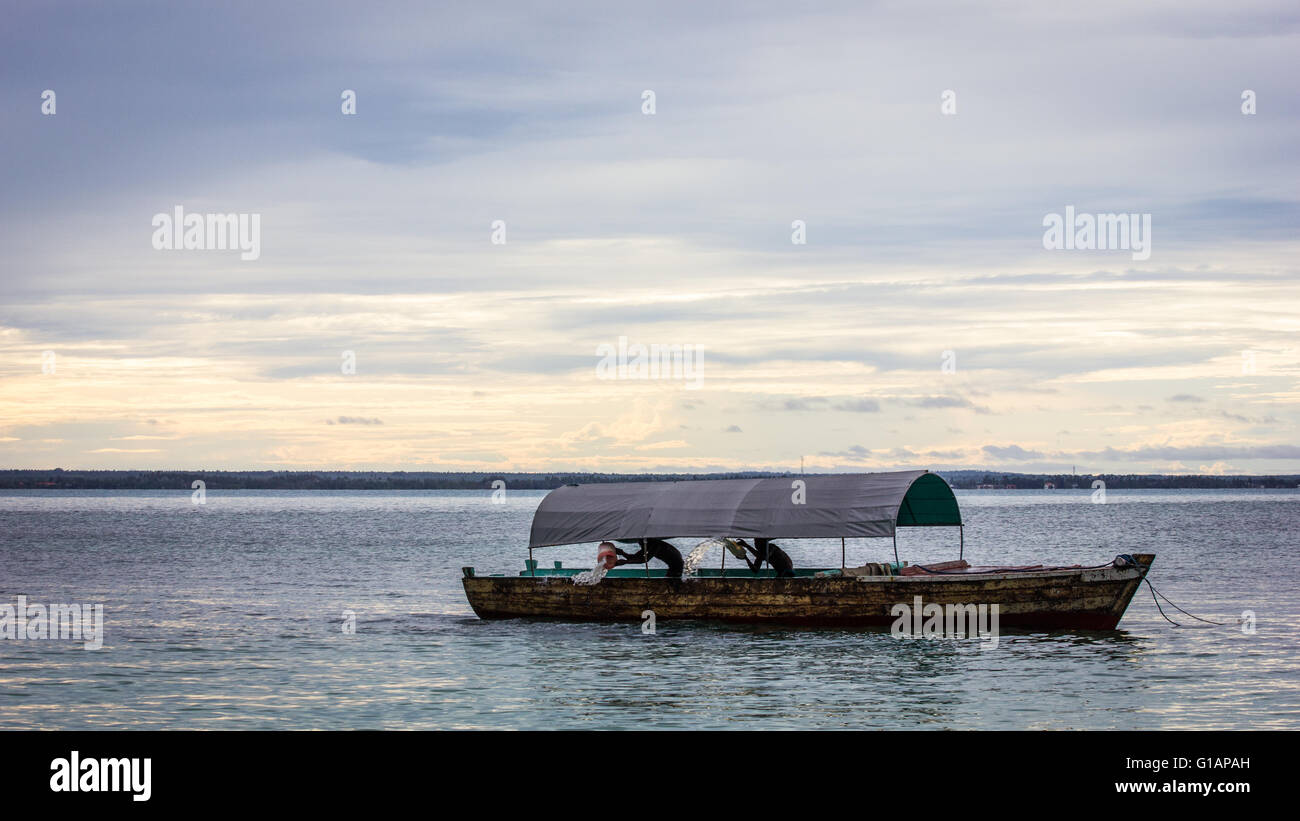 Two lone fishermen bail out their boat in the Indian Ocean, Zanzibar ...