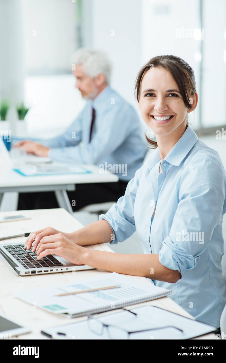 Smiling young business woman sitting at office desk and working with a ...