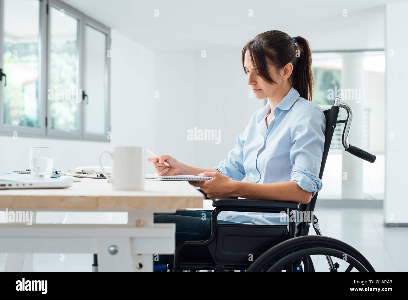 Confident disabled business woman in wheelchair working at office desk ...