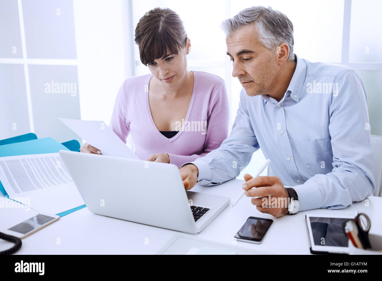 Executive working at office desk with his young assistant, they are ...