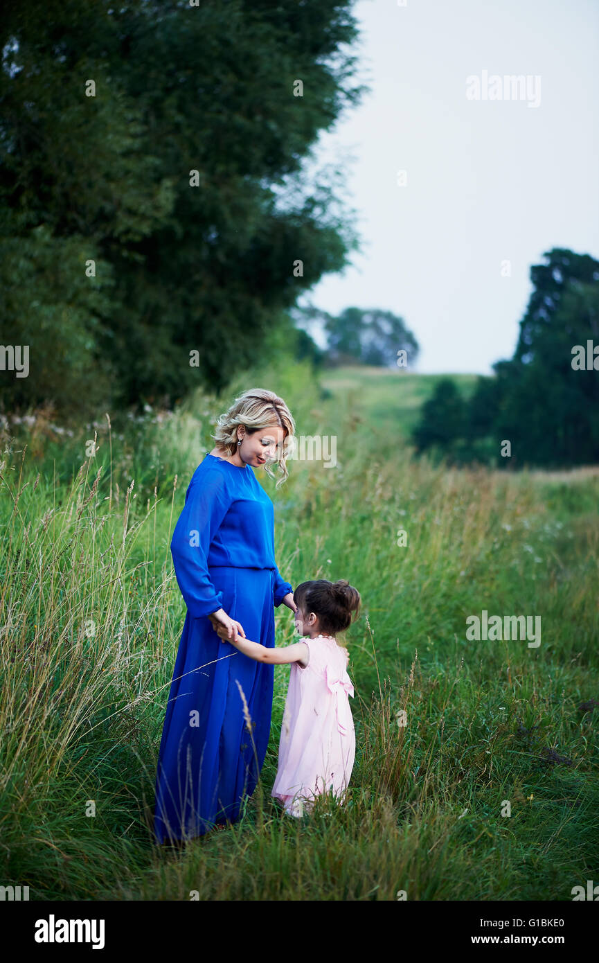 mother and daughter walk along the path among fields, holding hands ...