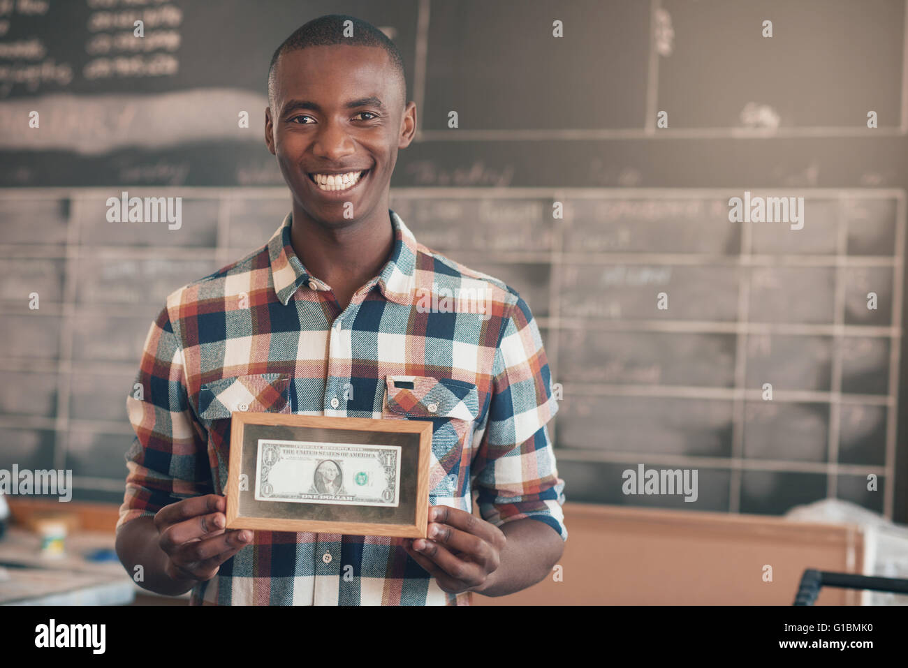 Smiling young business owner of African descent holding a framed dollar ...