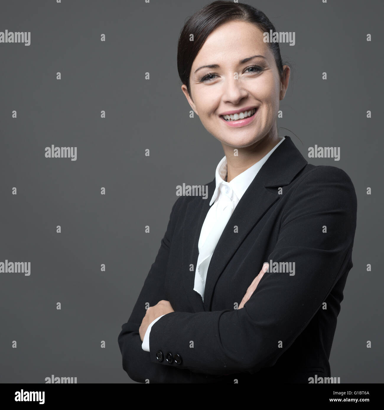 Confident attractive business woman with arms crossed posing on gray ...