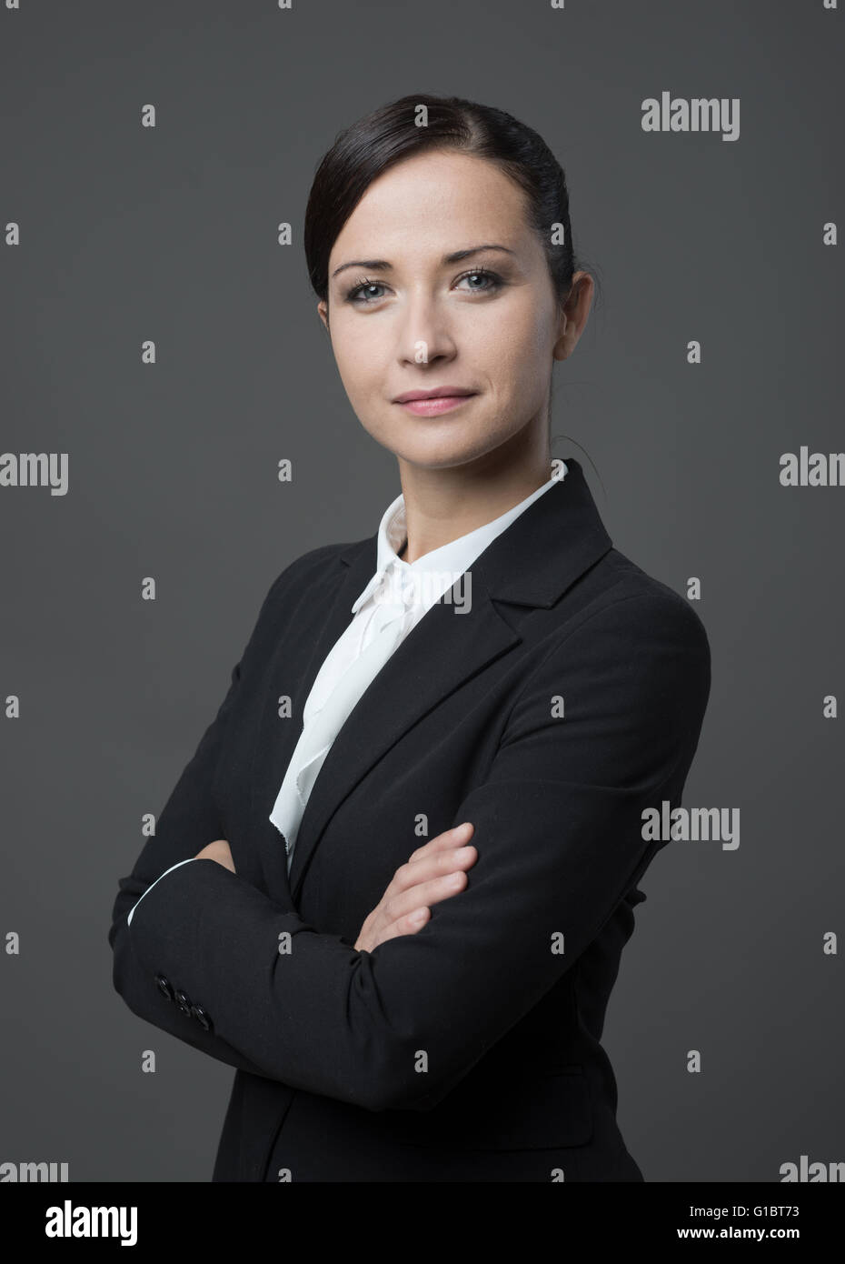 Confident female manager posing with arms crossed on gray background ...
