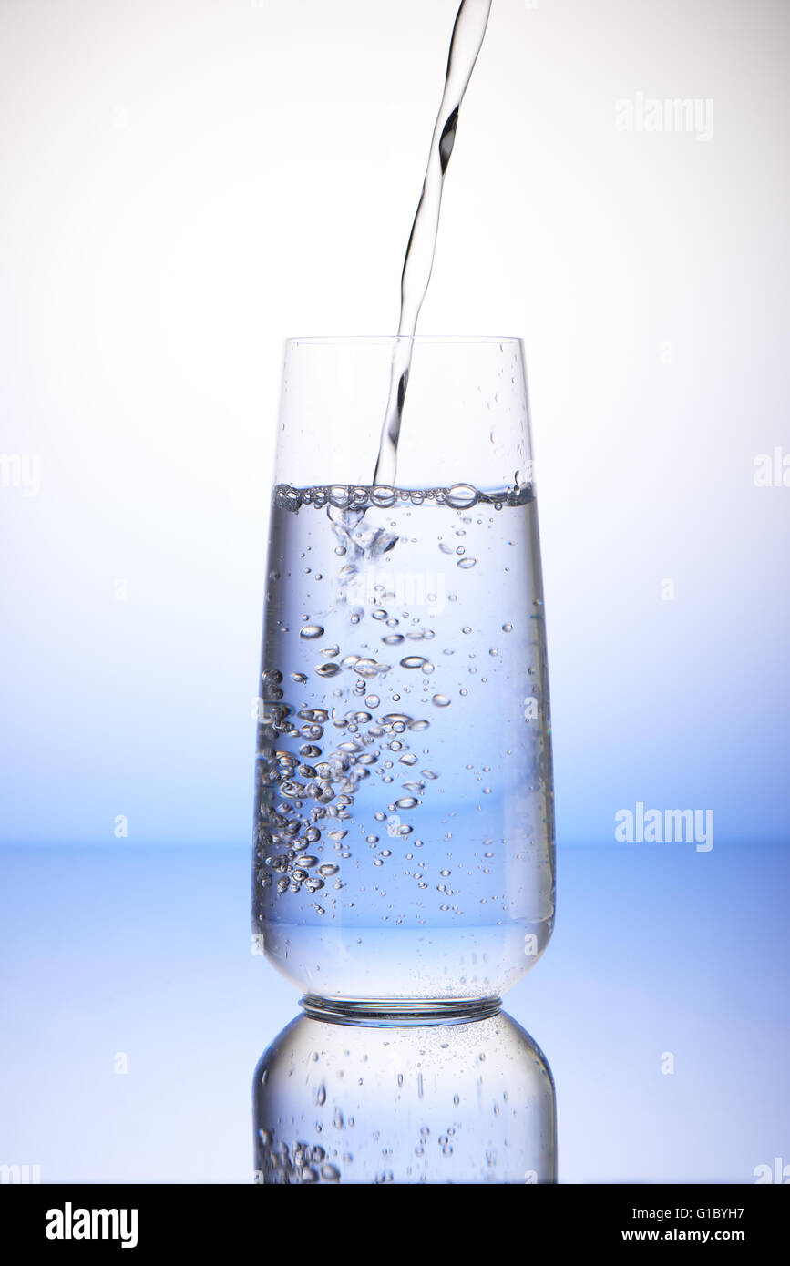Water pouring into two-thirds full drinking glass with reflection on ...