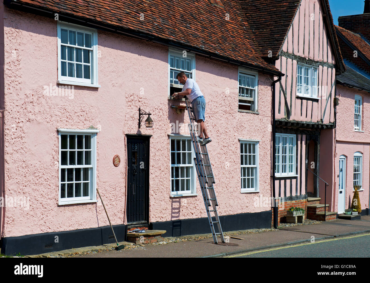 Man on ladder, repairing window frames on house in the village of ...