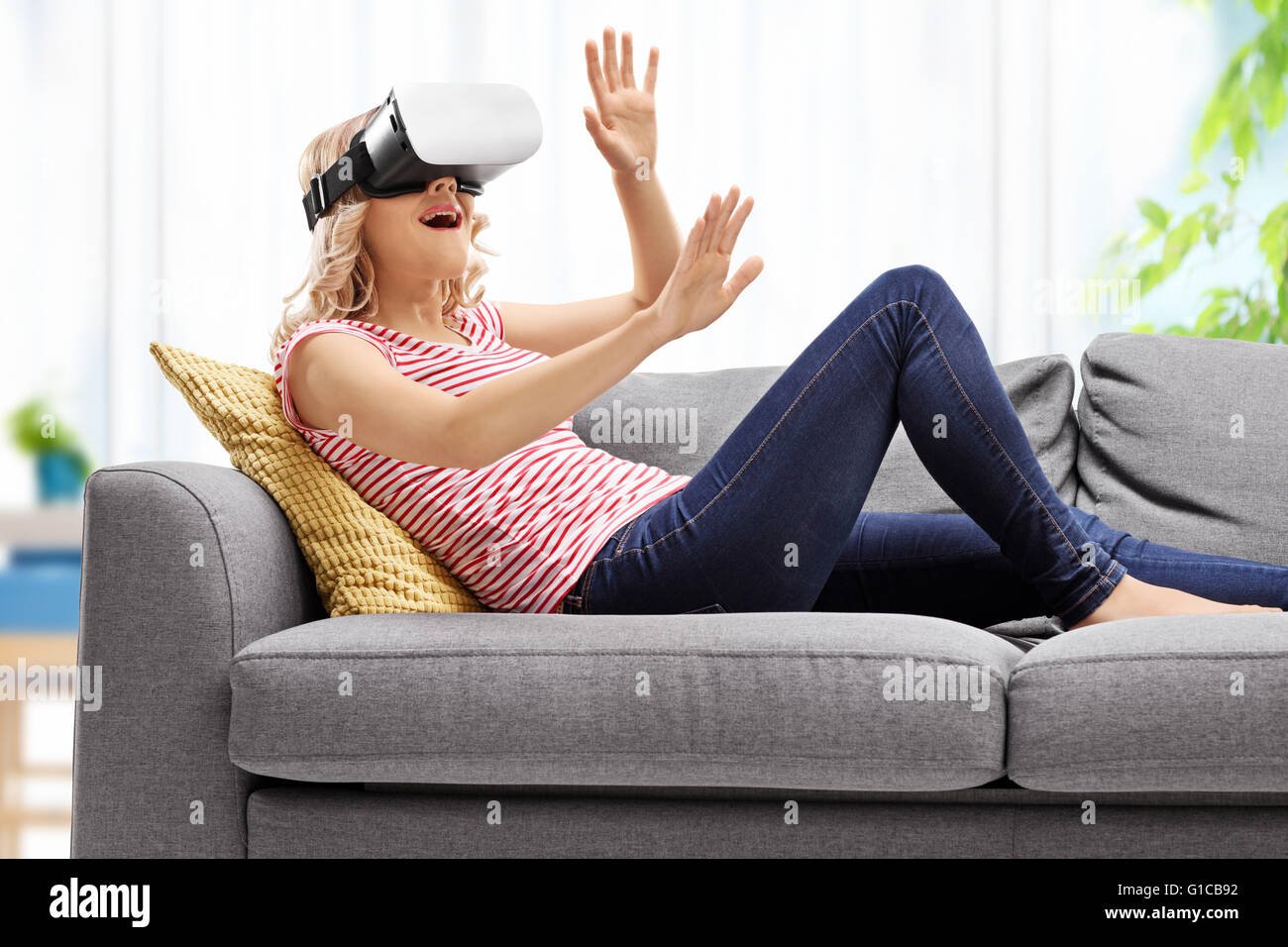 Young woman experiencing virtual reality seated on a couch at home ...