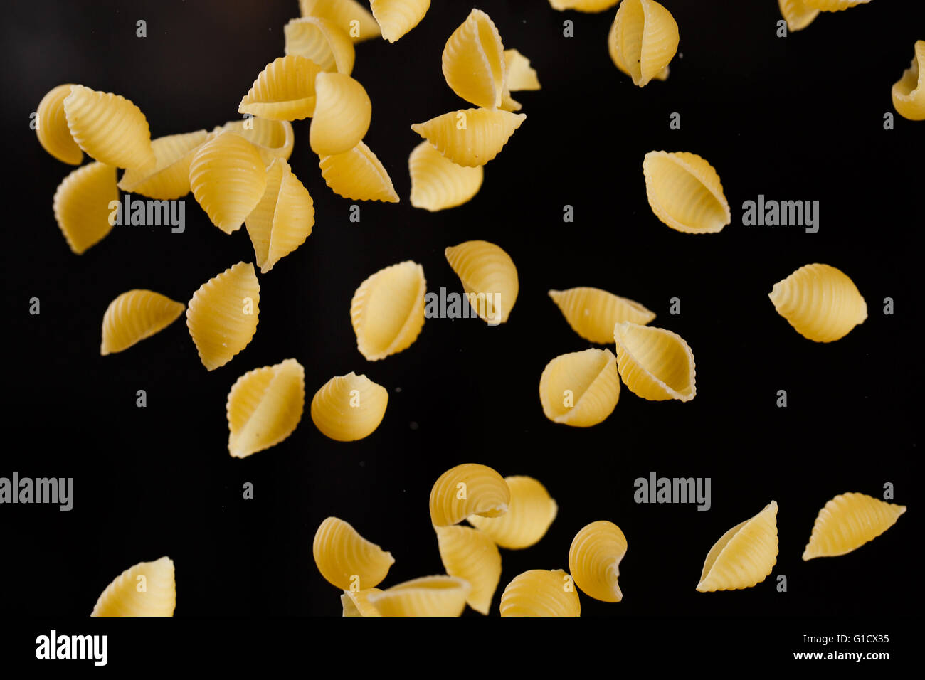 Falling conchiglie pasta. Flying yellow raw macaroni over black ...