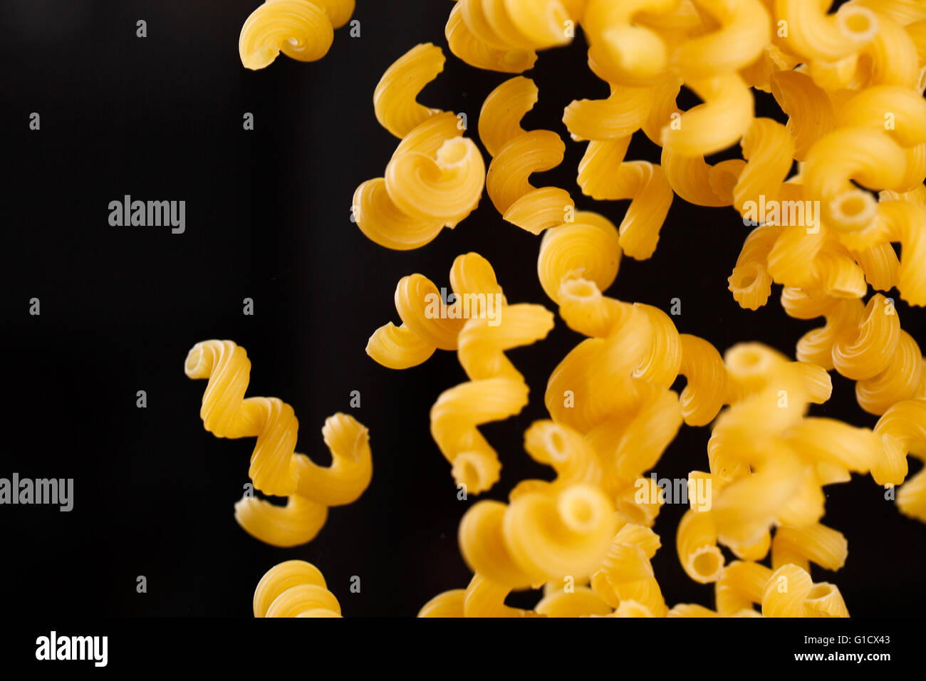 Falling cavatappi pasta. Flying yellow raw macaroni over black ...