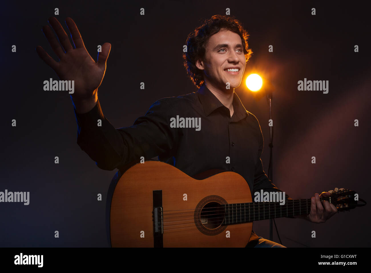Happy man holding guitar and waving hand over dark background Stock ...