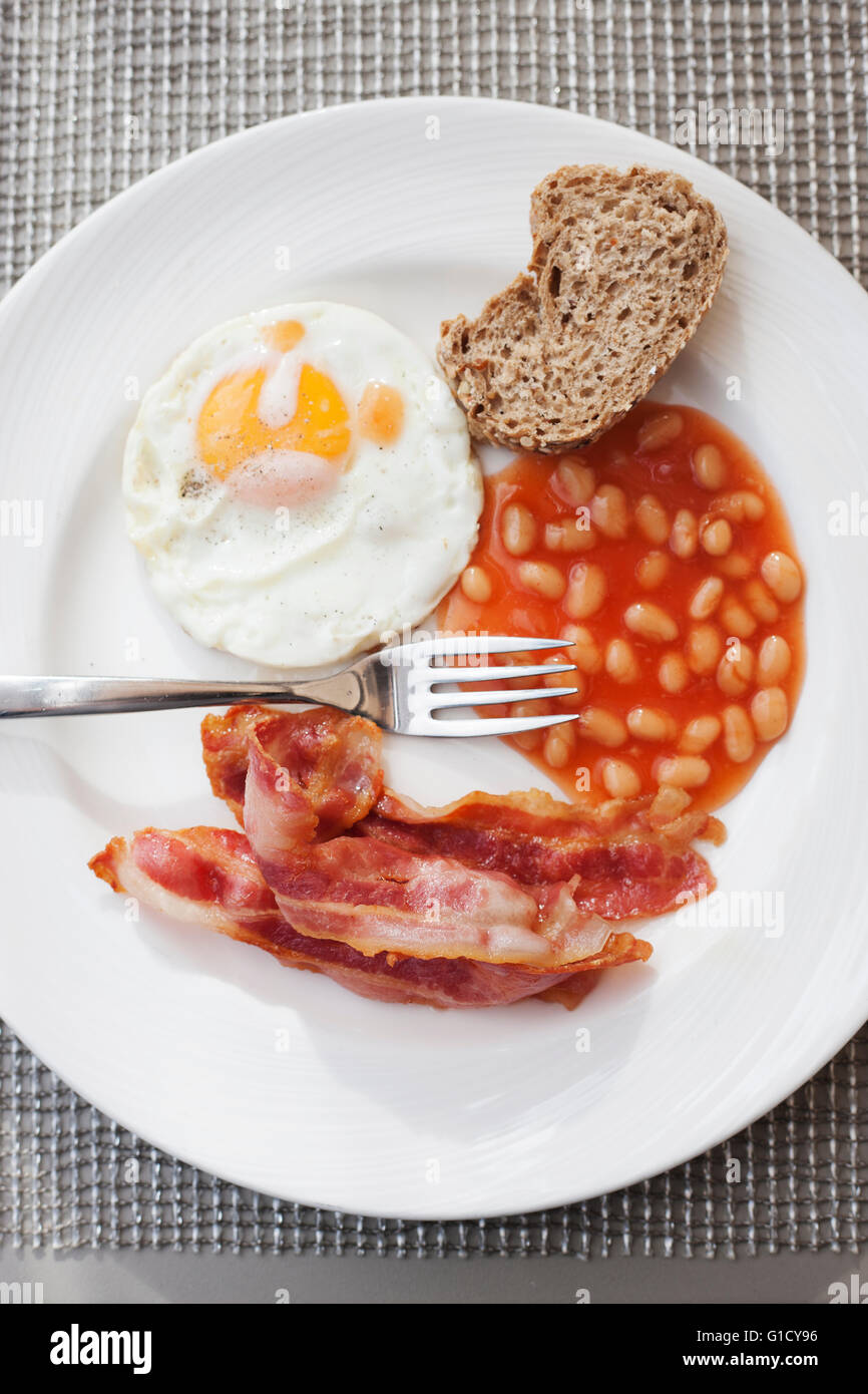 Plate of English fried breakfast consisting of fried egg, baked beans ...