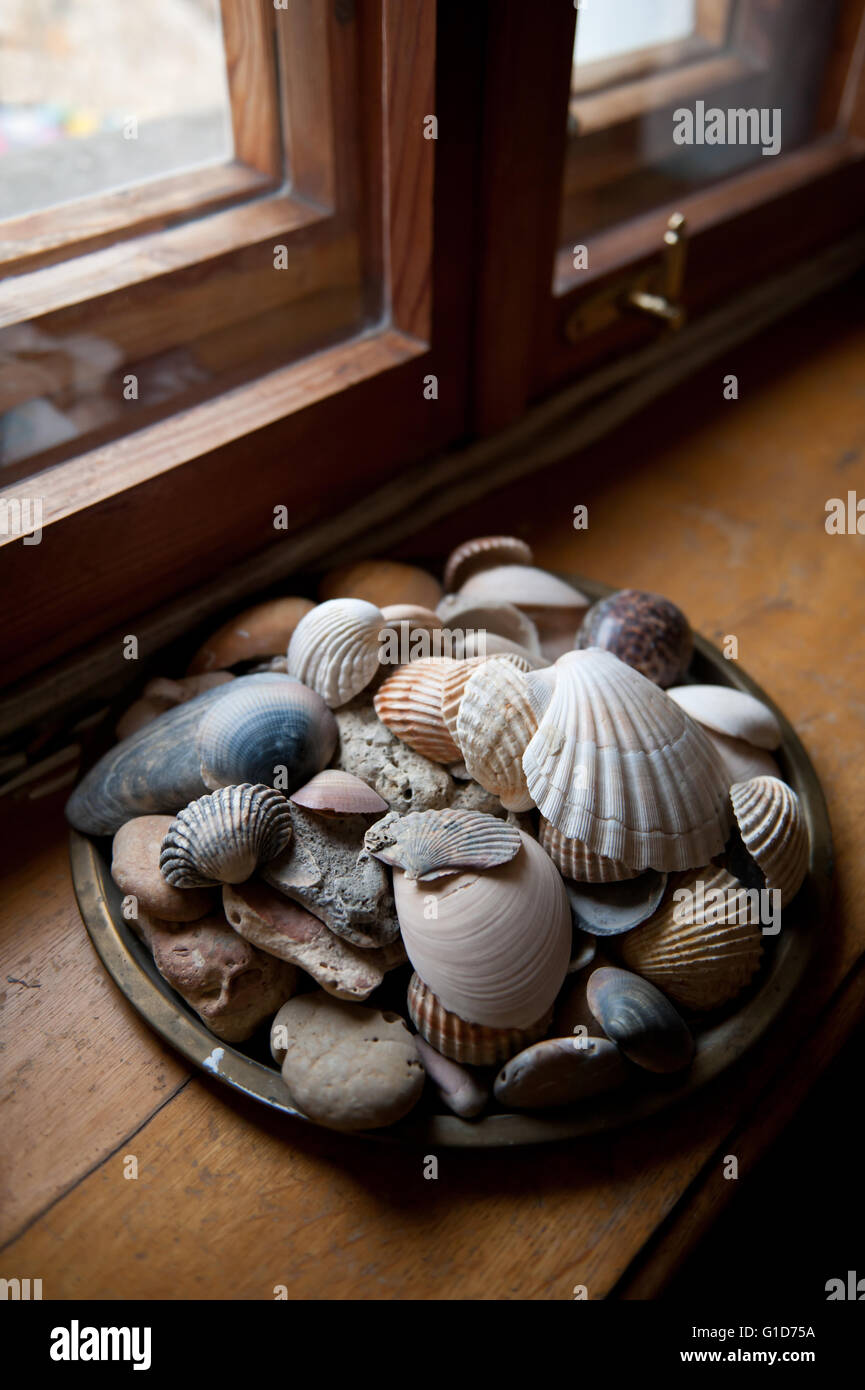 Sea shells and stones on windowsill in house interior, plate with ...