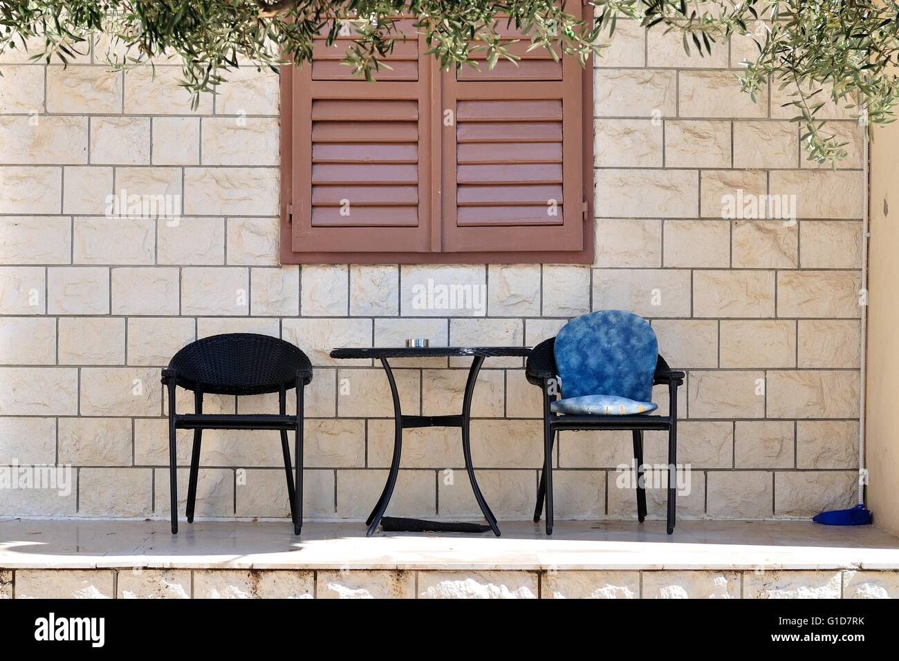 Table with two chairs in front of house wall with brown closed shutters ...